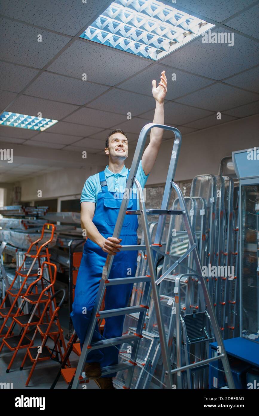 Male worker in uniform standing on stepladder in tool store. Department ...