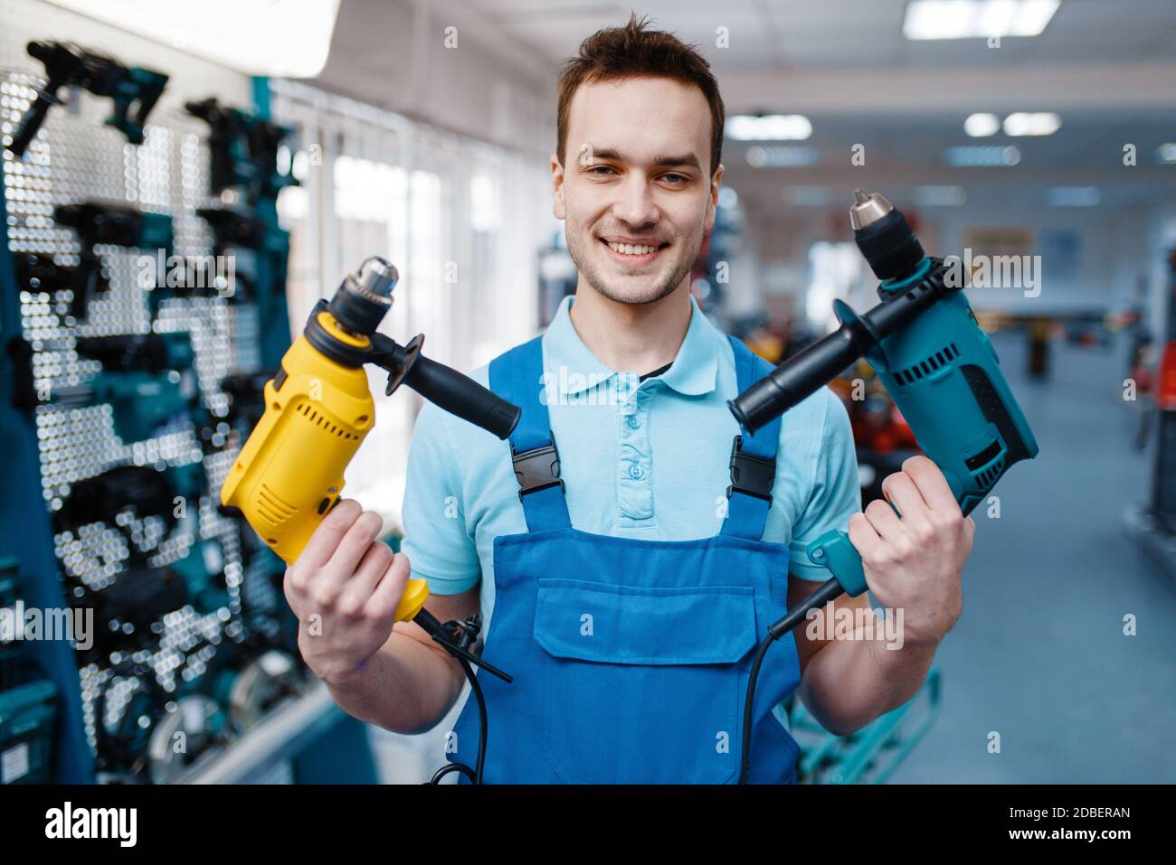Male worker in uniform holds two electric drills in tool store. Choice ...
