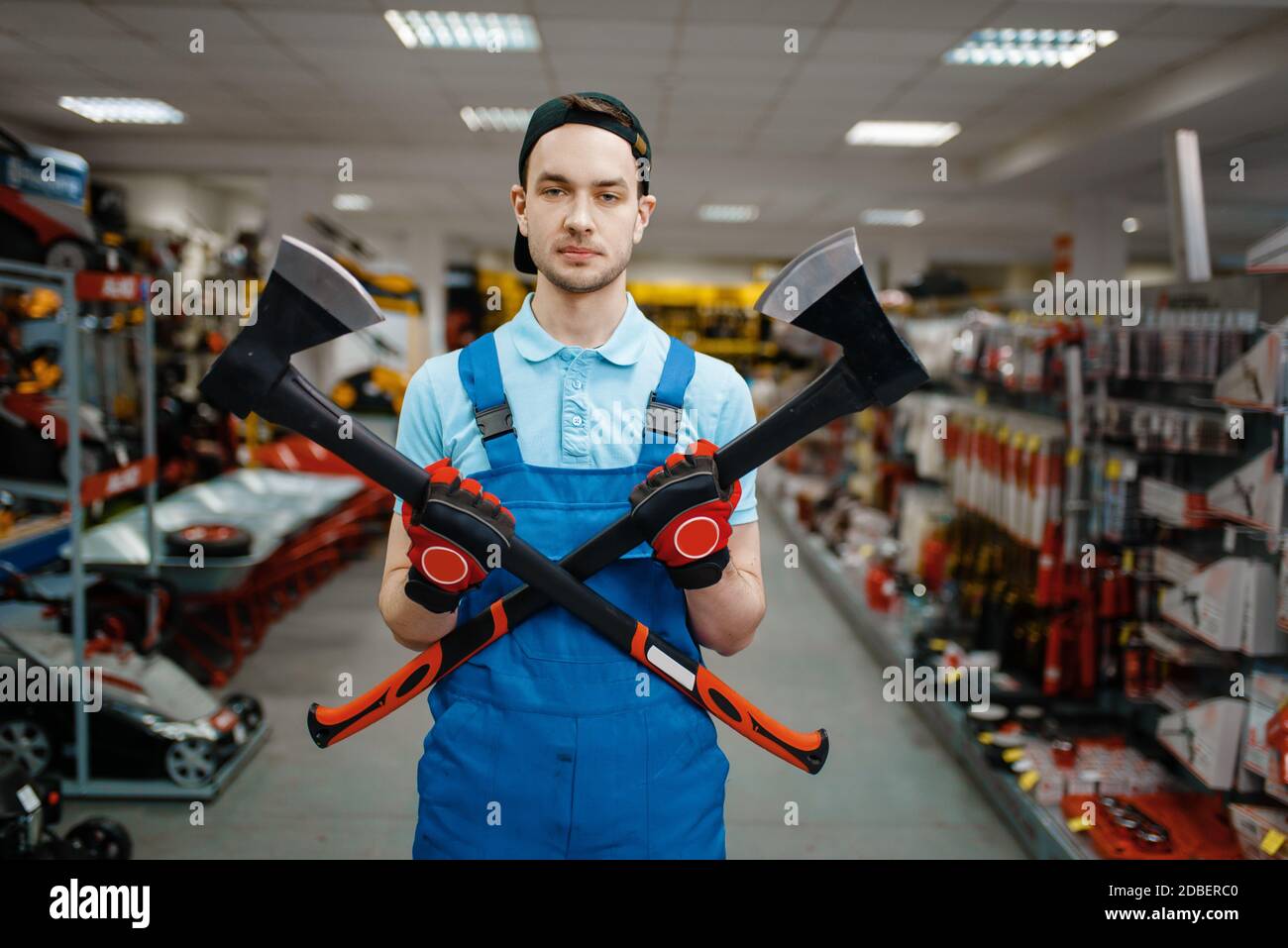Male worker in uniform holds two axes in tool store. Choice of ...