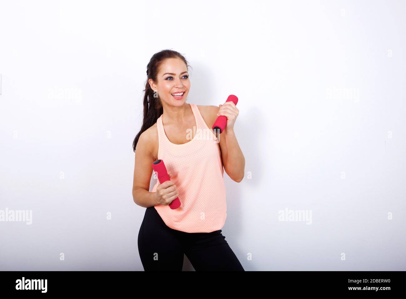 Portrait of smiling active woman lifting weights against white ...
