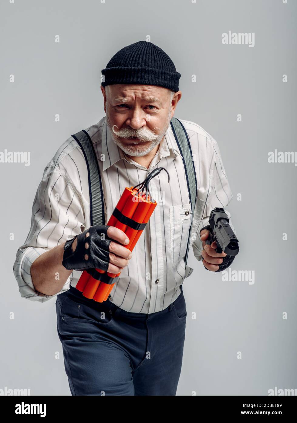 Elderly robber poses with dynamite and gun on grey background, gangster ...