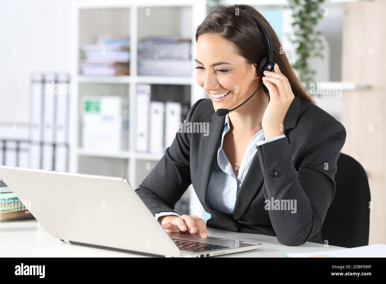 Happy telemarketer woman with laptop attending call with headset ...