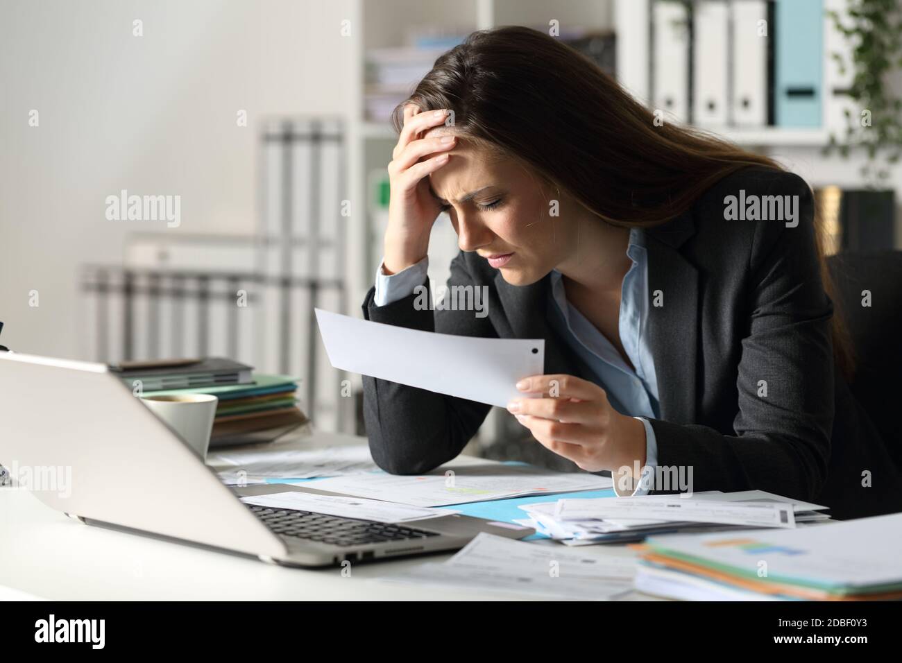 Sad executive woman complaining holding receipt sitting on her desk at ...