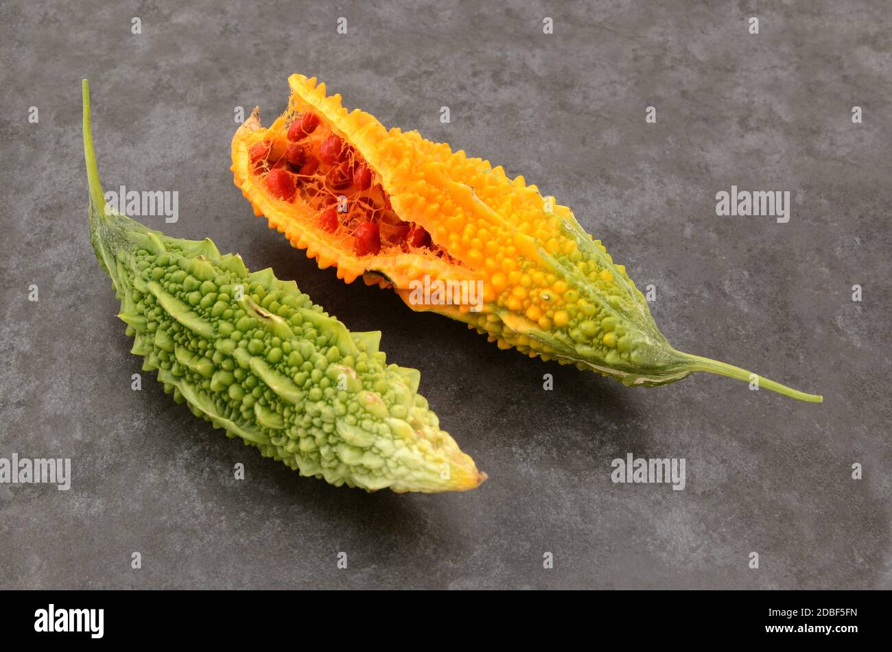Two ripe bitter melons - split orange with red seeds, and warty green ...