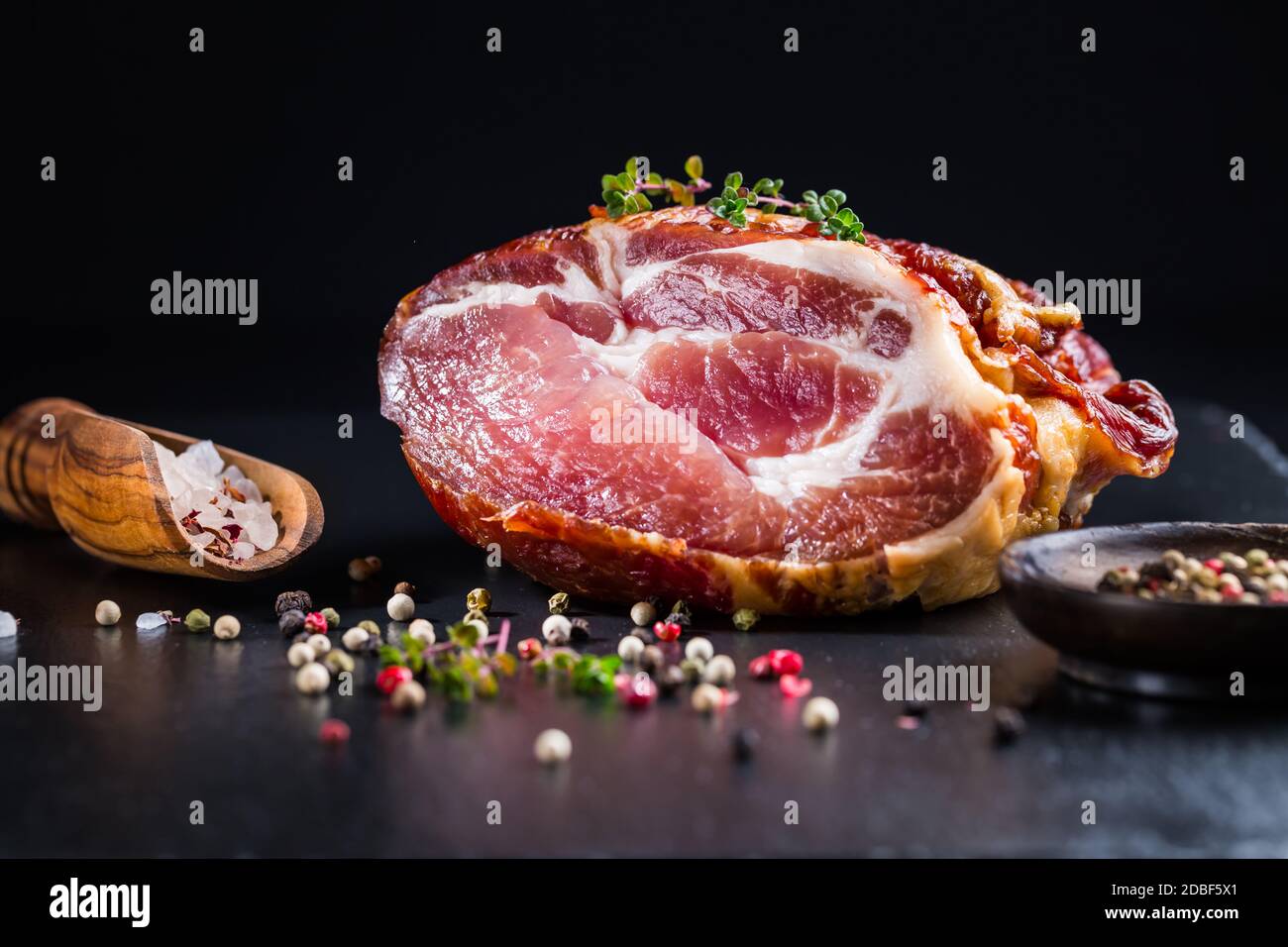Piece of smoked ham with pepper and herbs on black background ...
