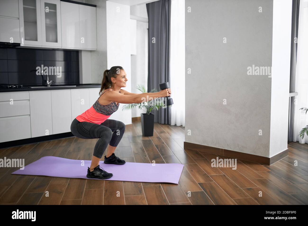 Side view of fit caucasian young woman squatting in kitchen and smiling ...