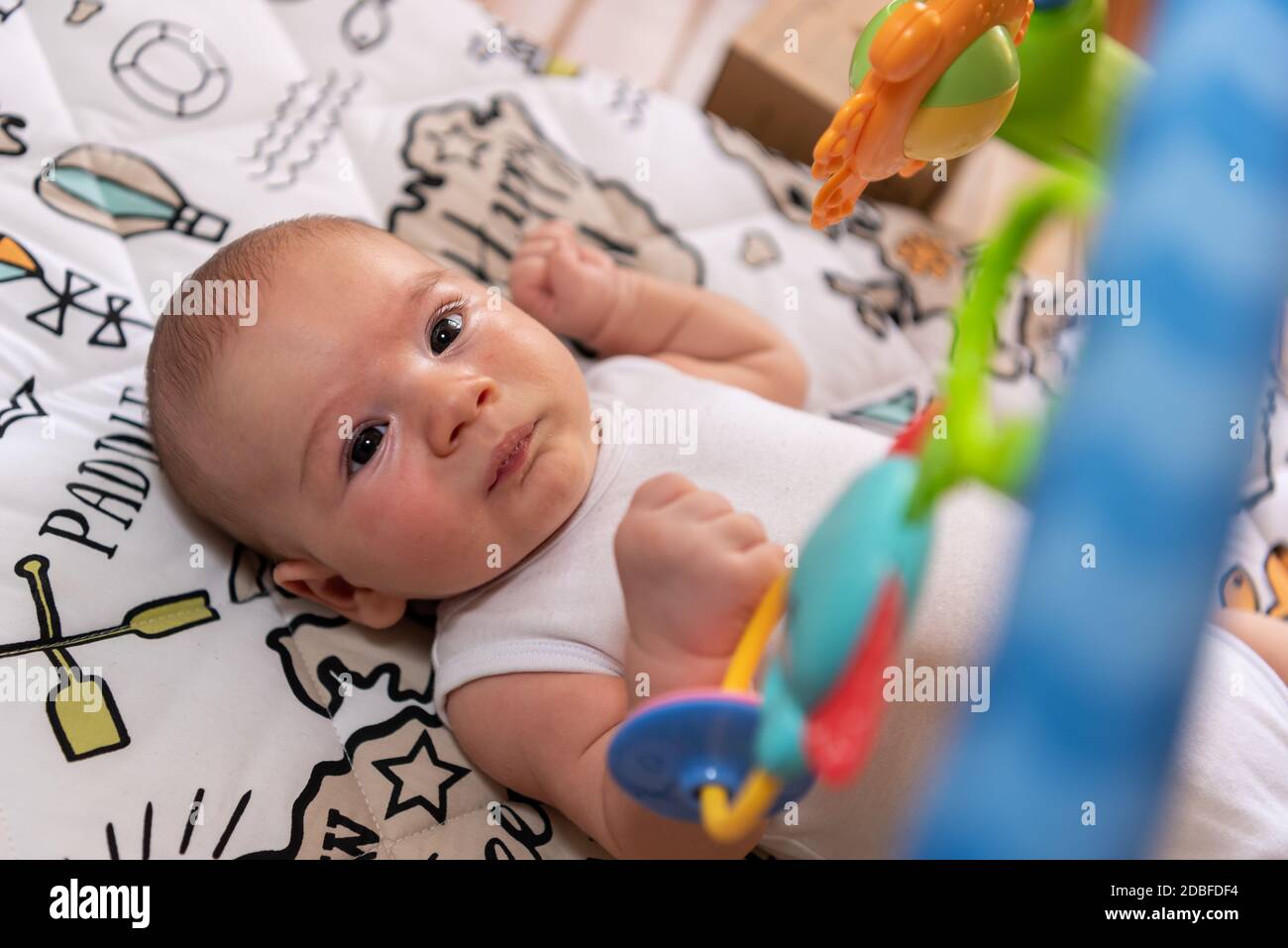 Adorable little baby boy lying on his back surrounded by colourful toys ...