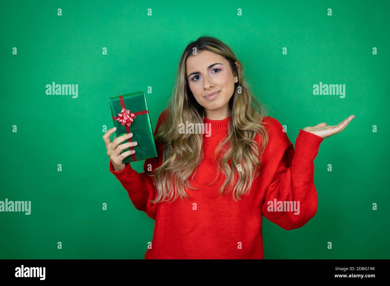 Young beautiful girl holding gift over isolated green background ...