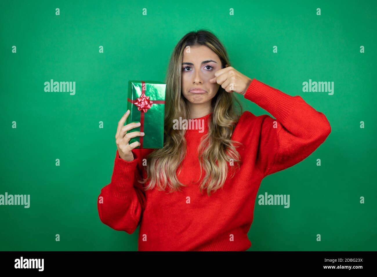 Young beautiful girl holding gift over isolated green background ...