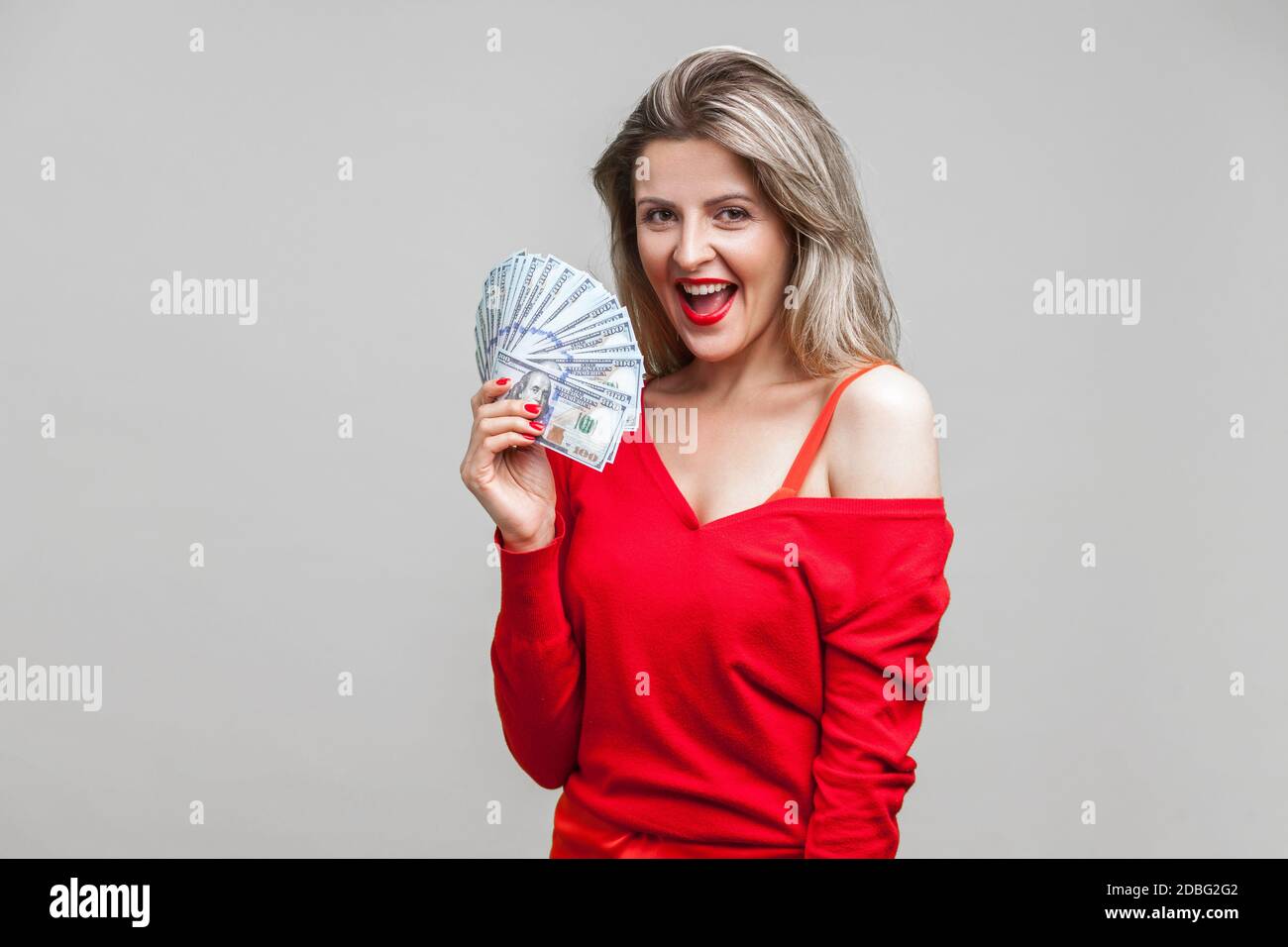 Portrait of amazed wealthy young woman in red dress standing, holding ...