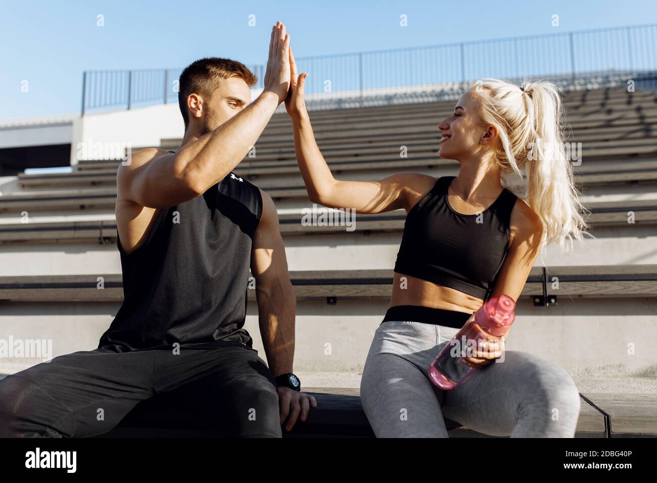 Sportive young couple, sitting on stairs outdoors and giving each other ...