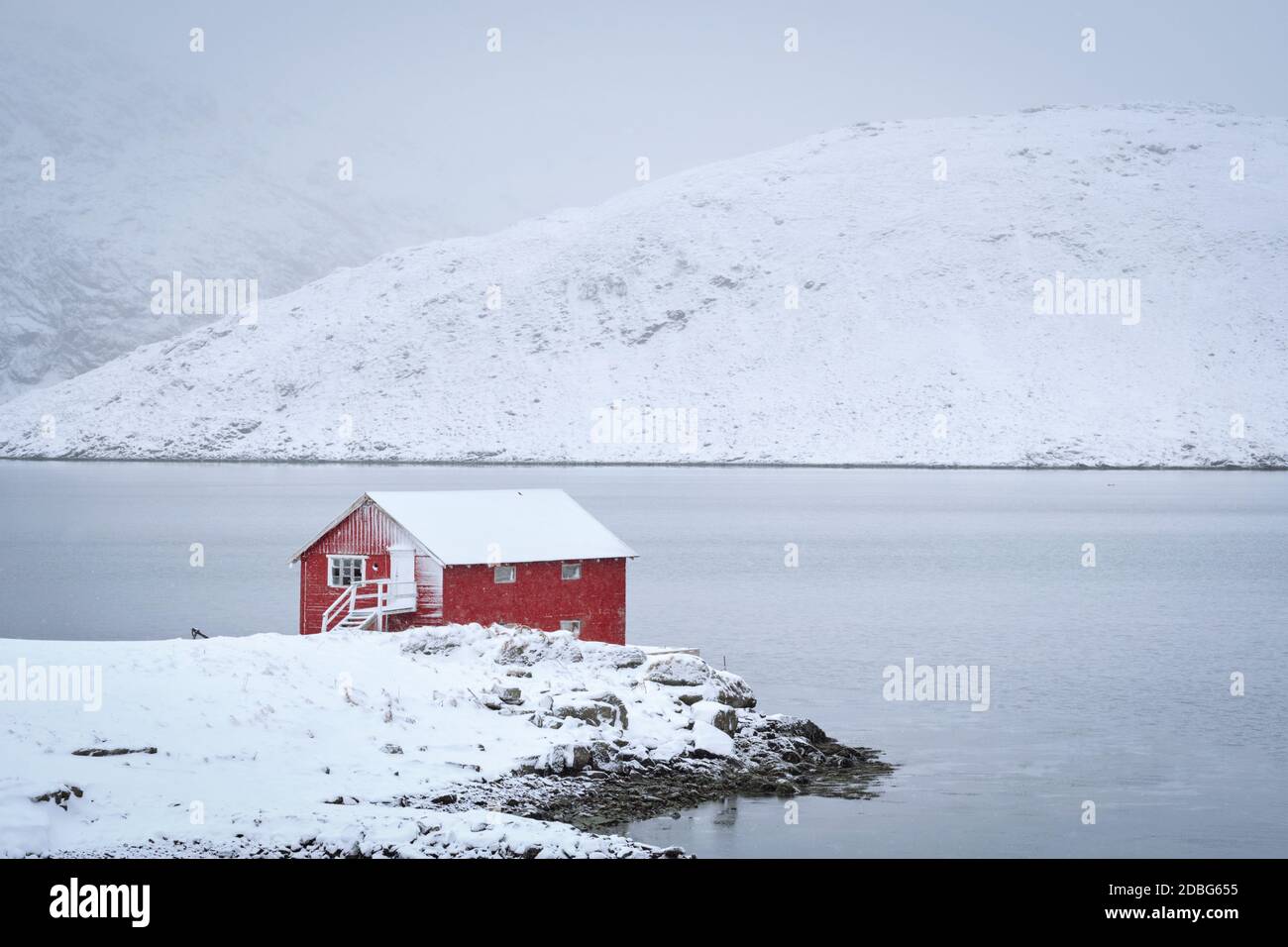 Traditional red rorbu house on fjord shore with heavy snow in winter ...