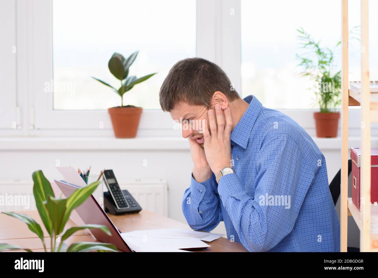Office clerk grimacing grimacing pain on his face looking at a laptop ...