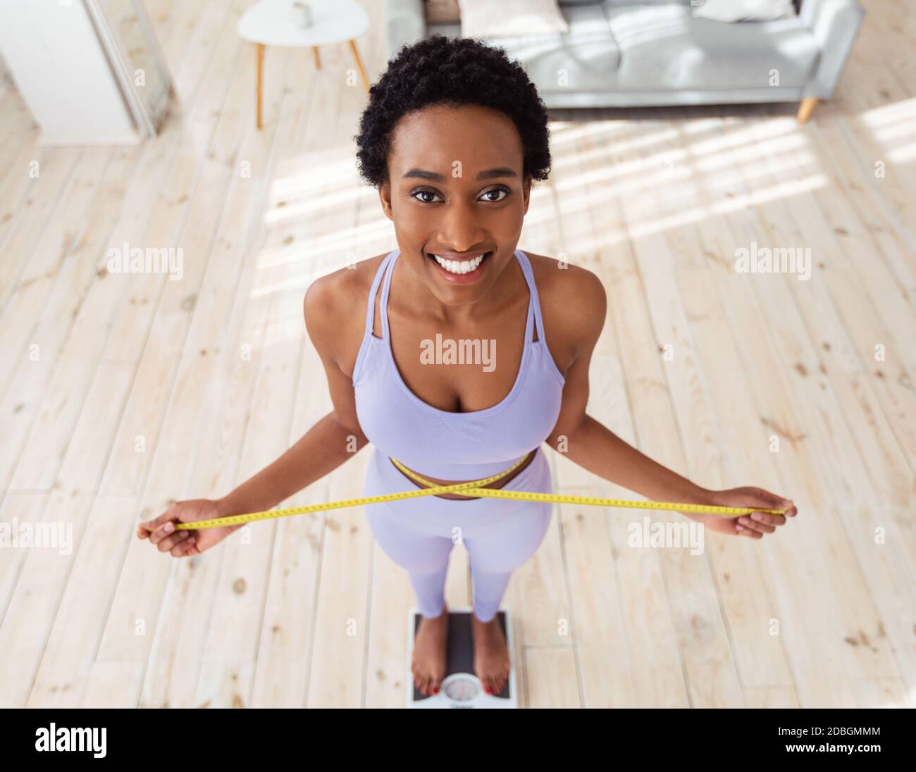 Above view of smiling young black woman standing on scales and ...