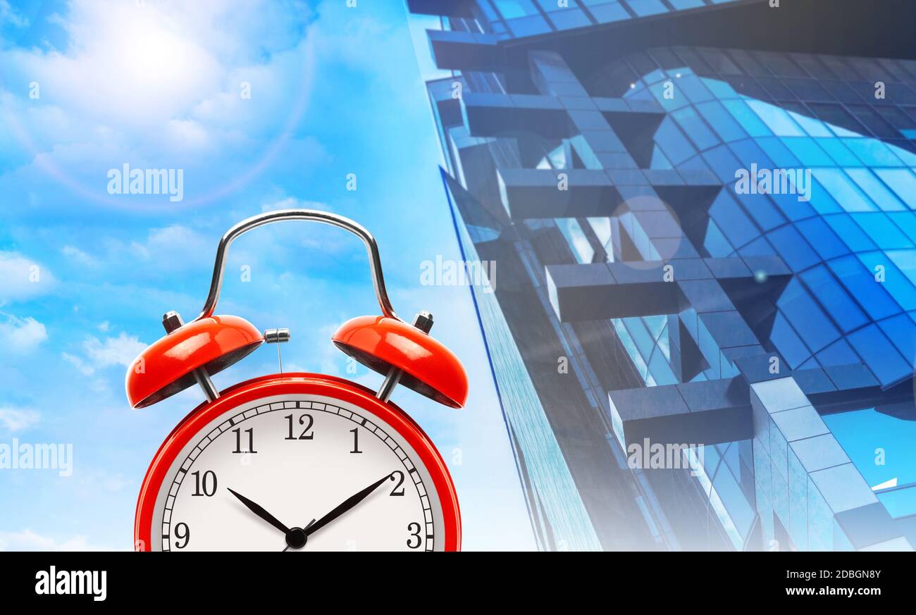 Red alarm clock on a modern townhouse and blue sky background. The ...