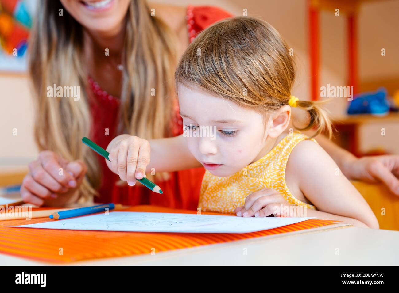 Children drawing with pencils in play school, the teacher helps Stock ...