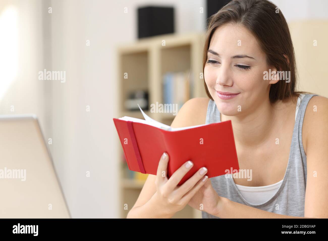 Happy woman reading notes on red agenda sitting on a desk at home Stock ...