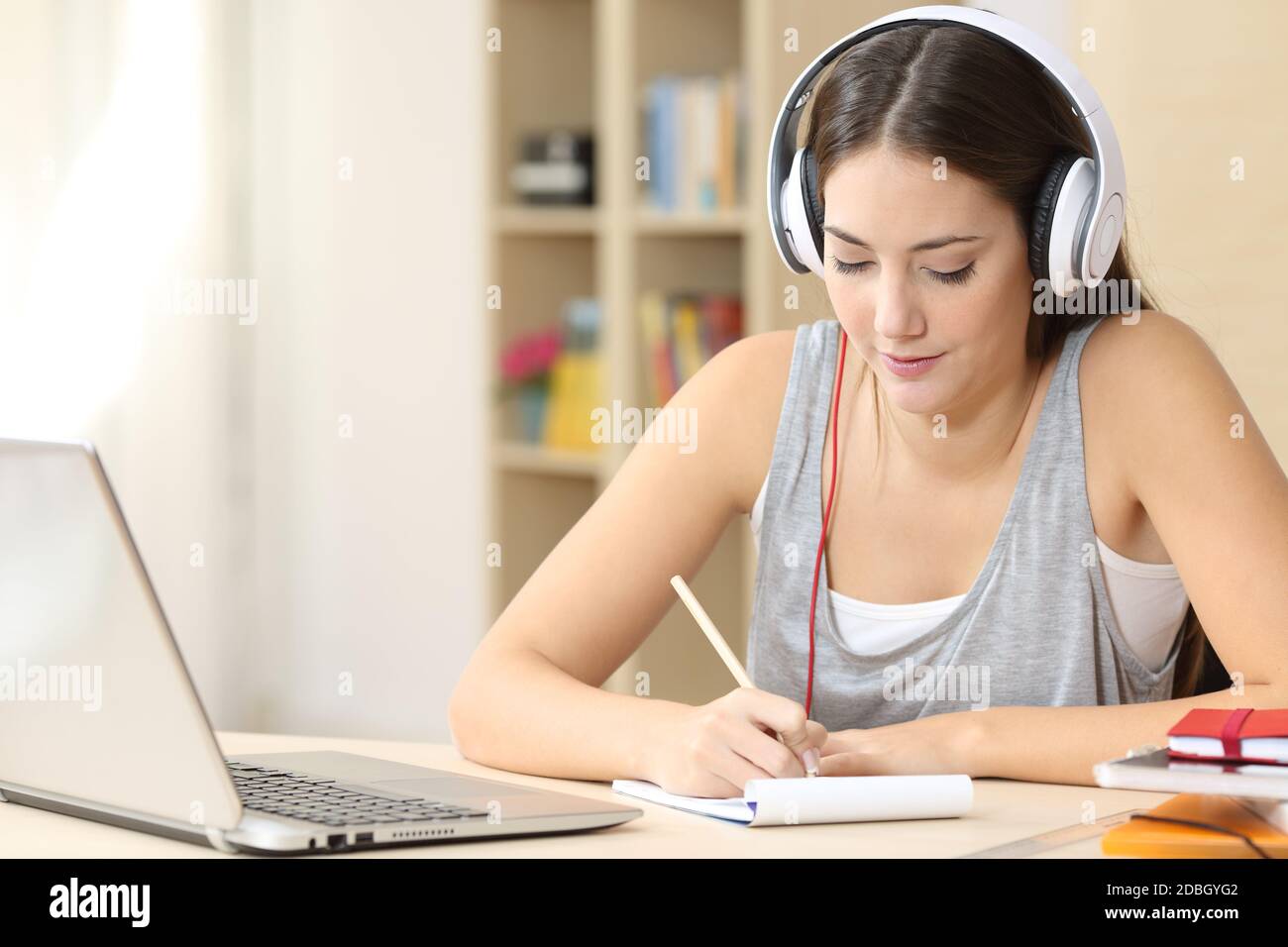 Serious student woman with headphones taking notes on notepad sitting ...