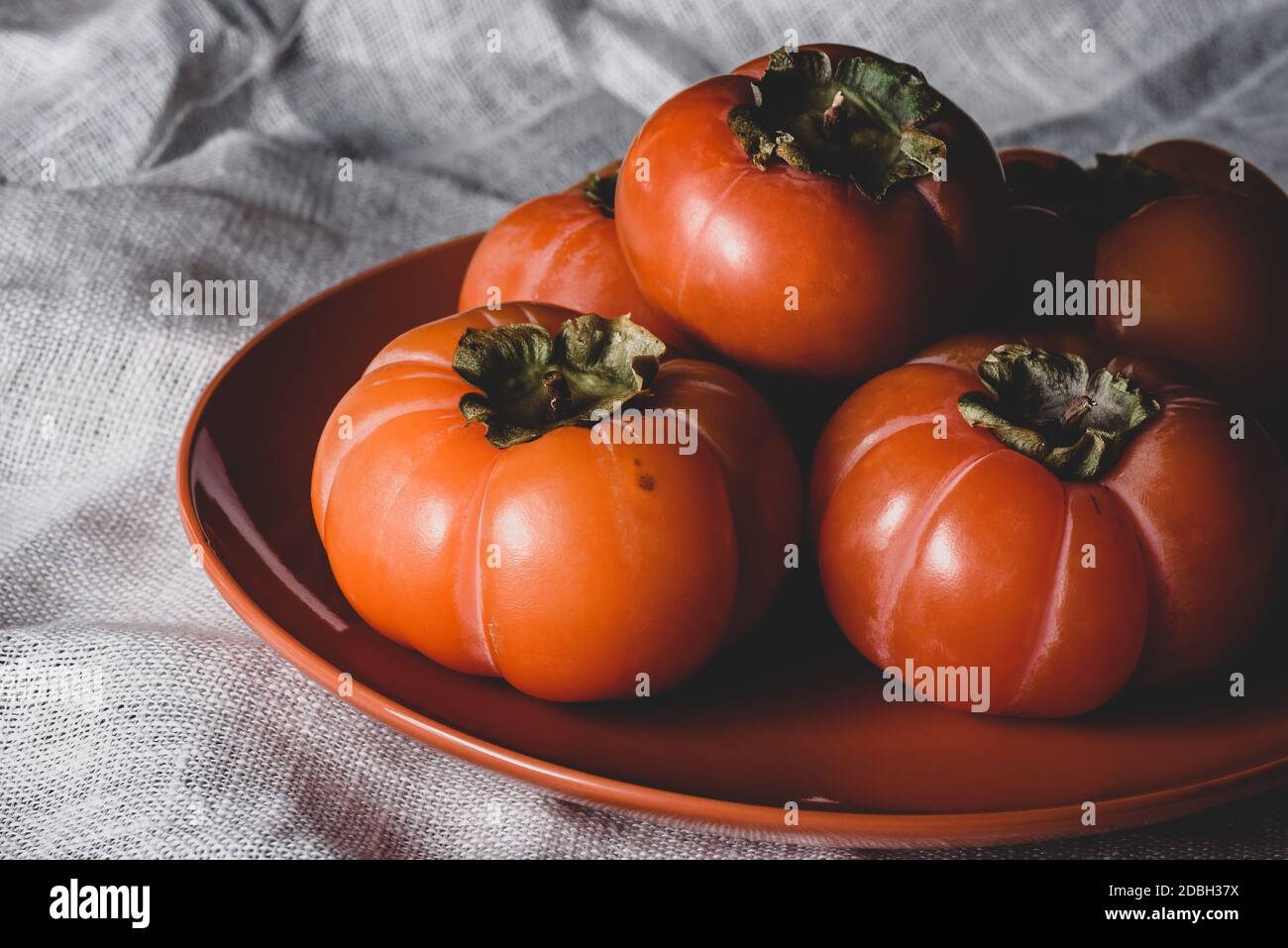 Few fresh persimmons on orange plate over white textile Stock Photo - Alamy