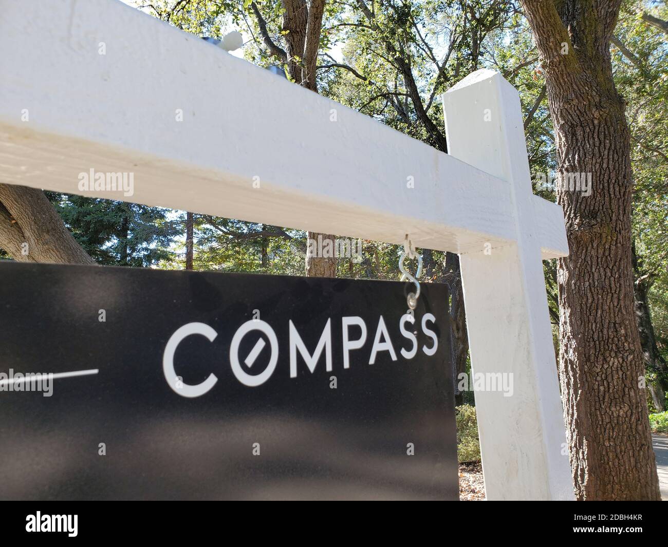 Close-up of a Compass Real Estate hanging sign panel in a wooded area ...