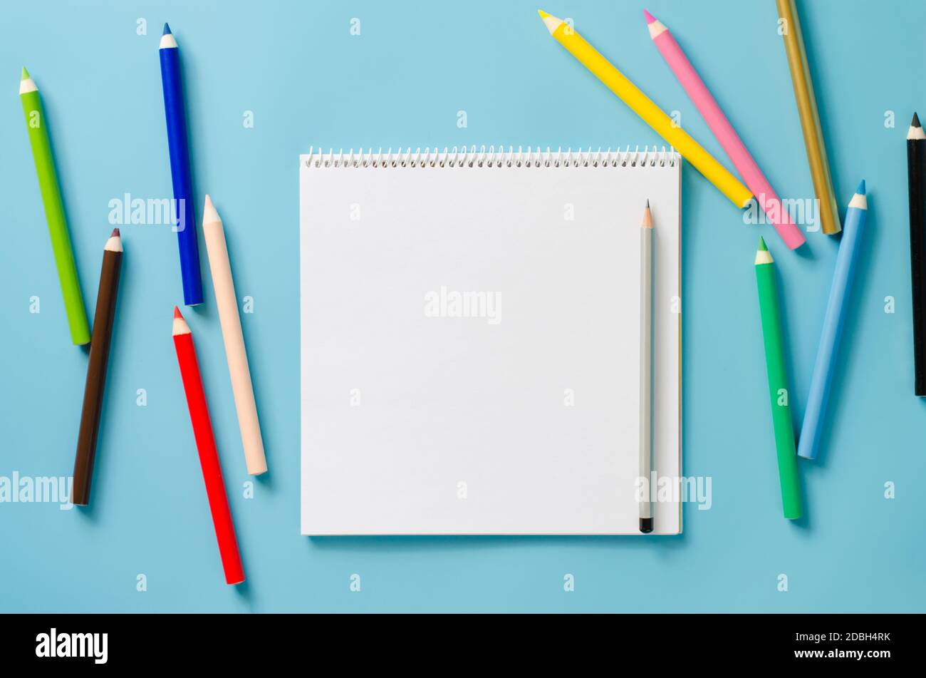 Empty square notebook and set of colorful pencils on blue background ...