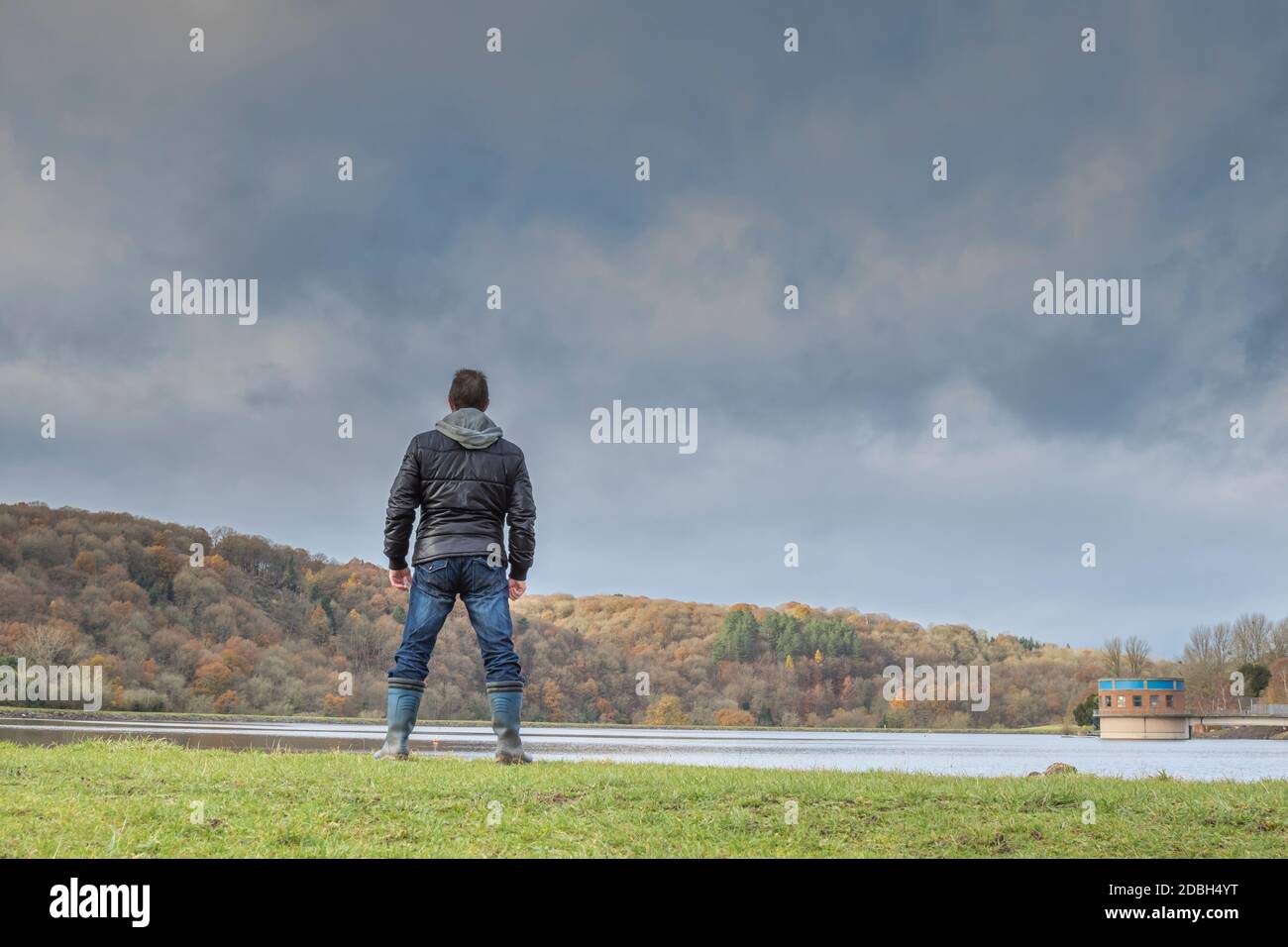 rear view of a menacing man looking over water with moody clouds above ...