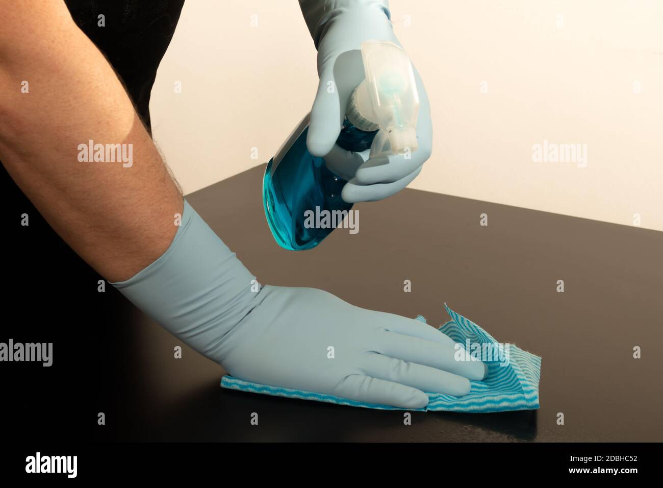 Gloved hands sanitizing a table. In one hand a cleaning cloth and in ...