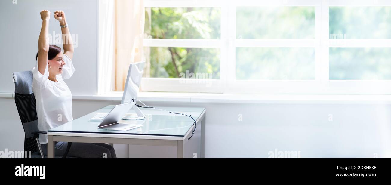 Happy Woman At Computer Desk With Hands Raised Stock Photo - Alamy