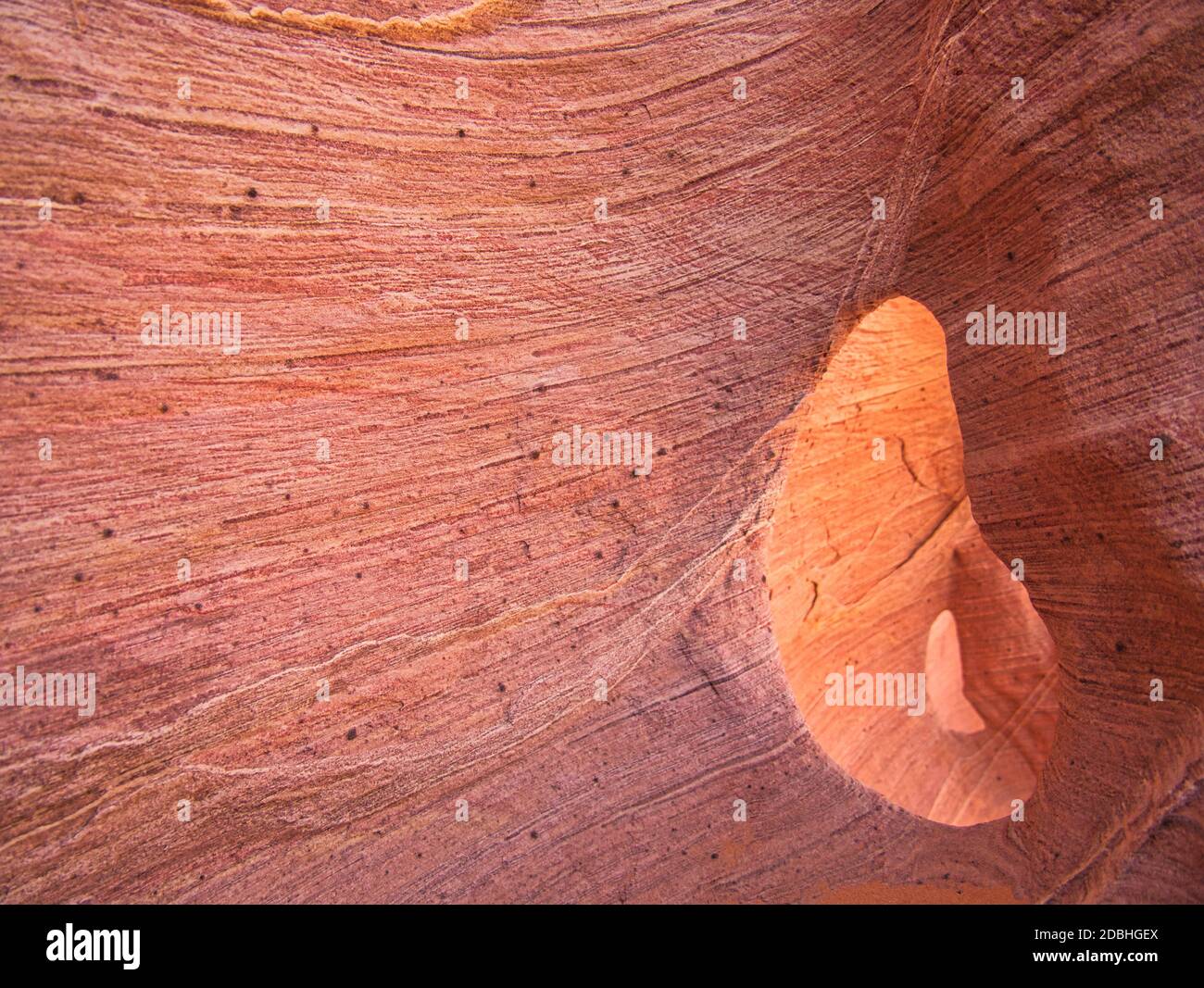 A red-brown rock face with rough lines and a small opening Stock Photo ...