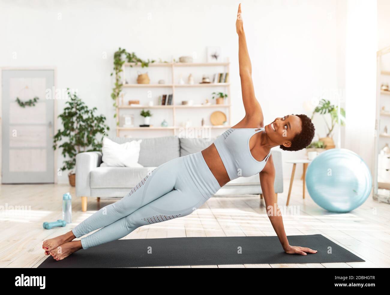 Attractive fit black lady standing in side plank on sports mat at home ...