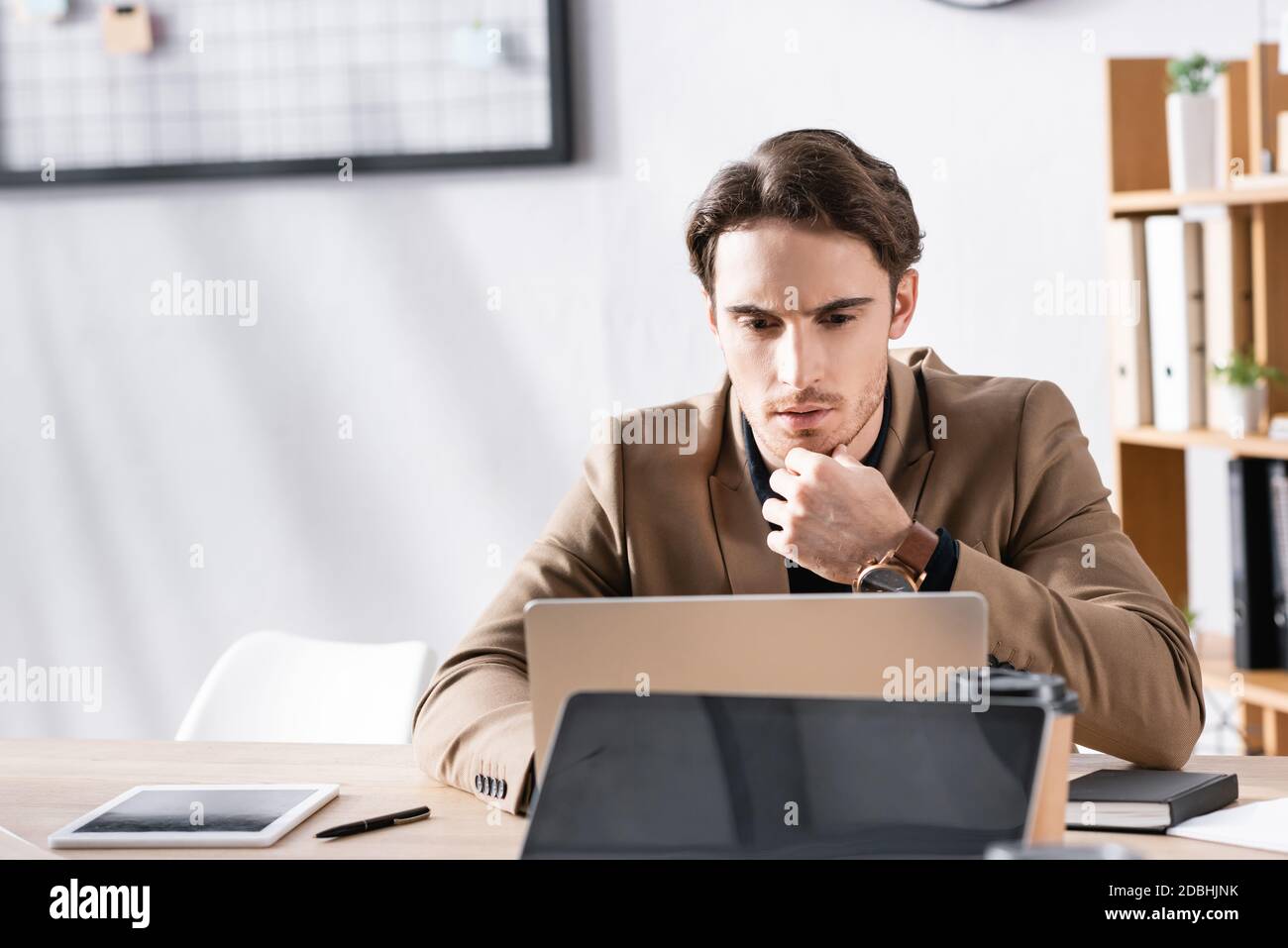 Thoughtful office worker looking at laptop while sitting at desk in ...
