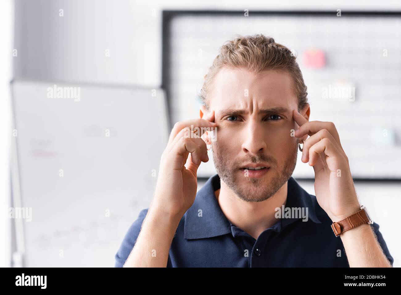 Exhausted office worker looking at camera, while touching head with ...