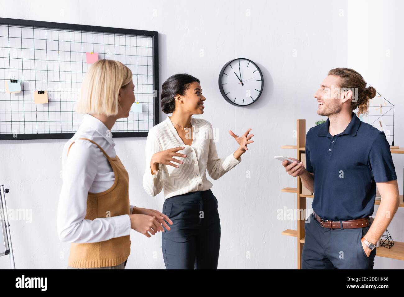 Happy multiethnic office workers gesturing and talking while standing ...
