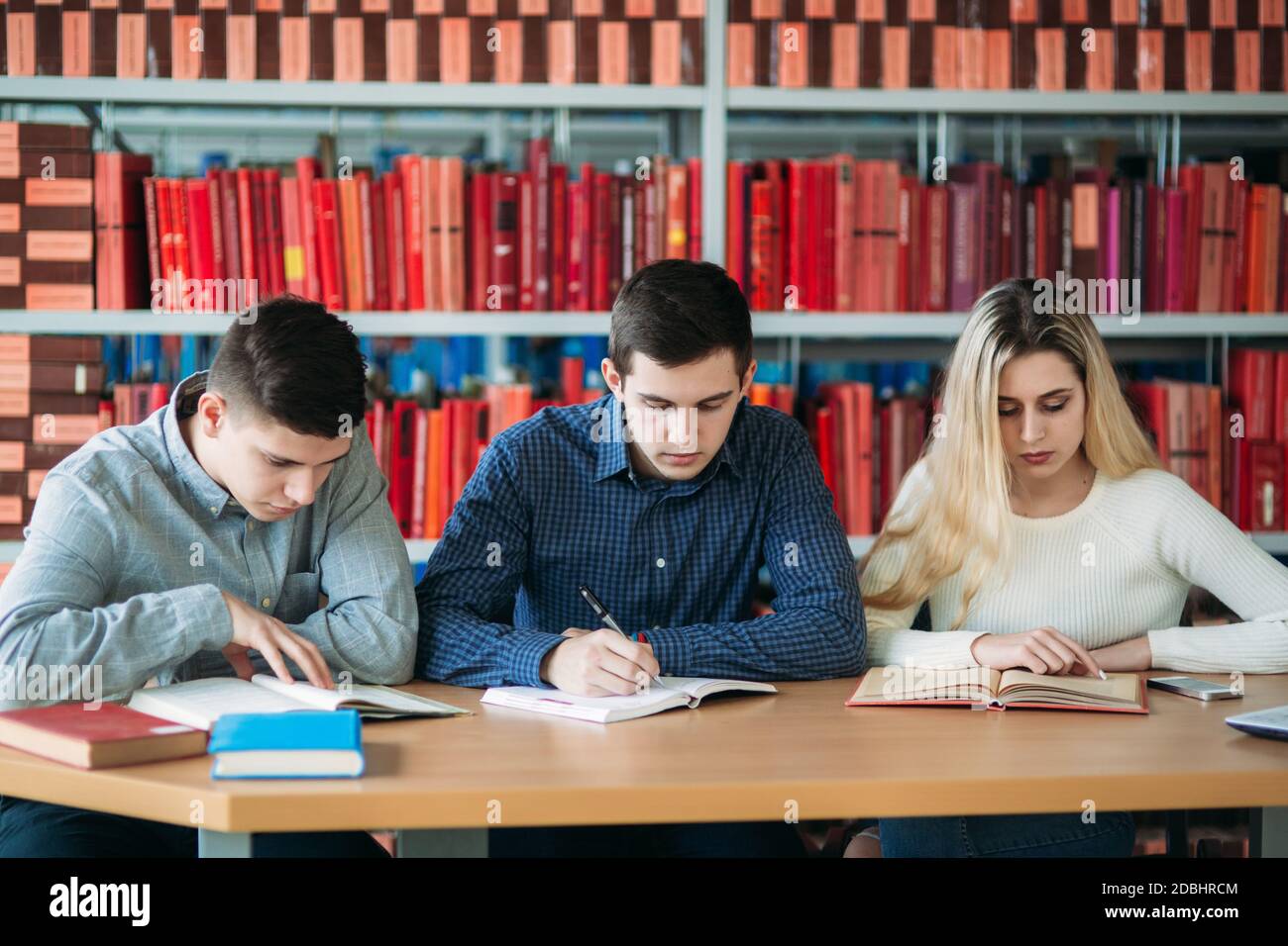 University students sitting together at table with books and laptop ...