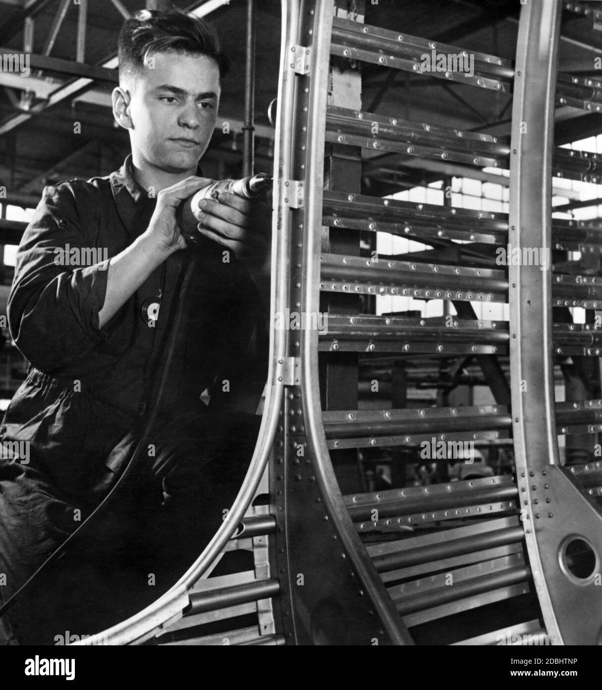 A young worker is drilling on an aircraft fuselage in one of the ...