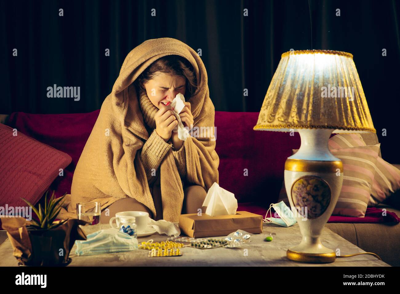 Sneezy. Young woman wrapped in a plaid looks sick, ill, sneezing and ...