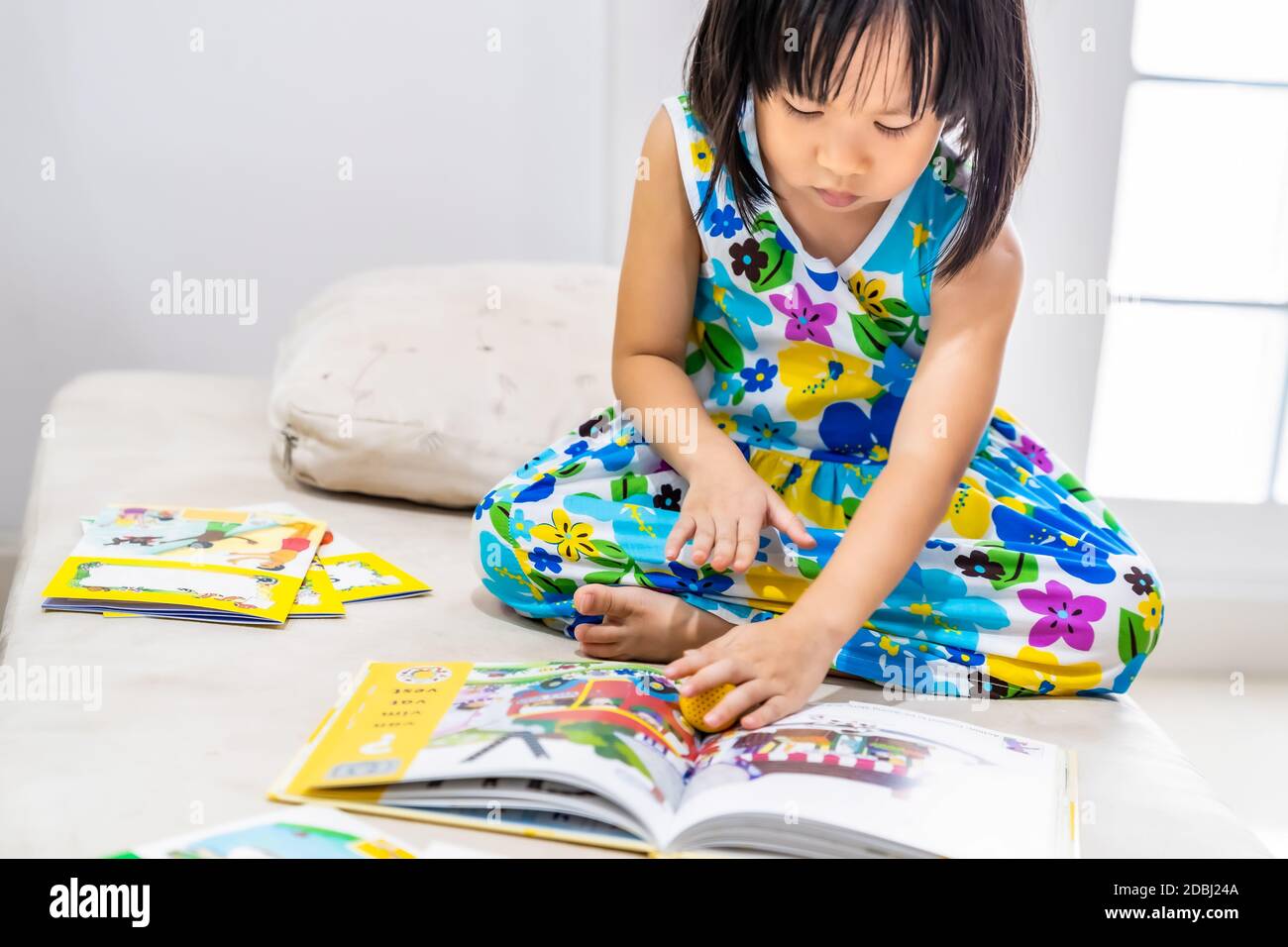 Asian girl child reading interactive book in living room at home as home schooling while city ...