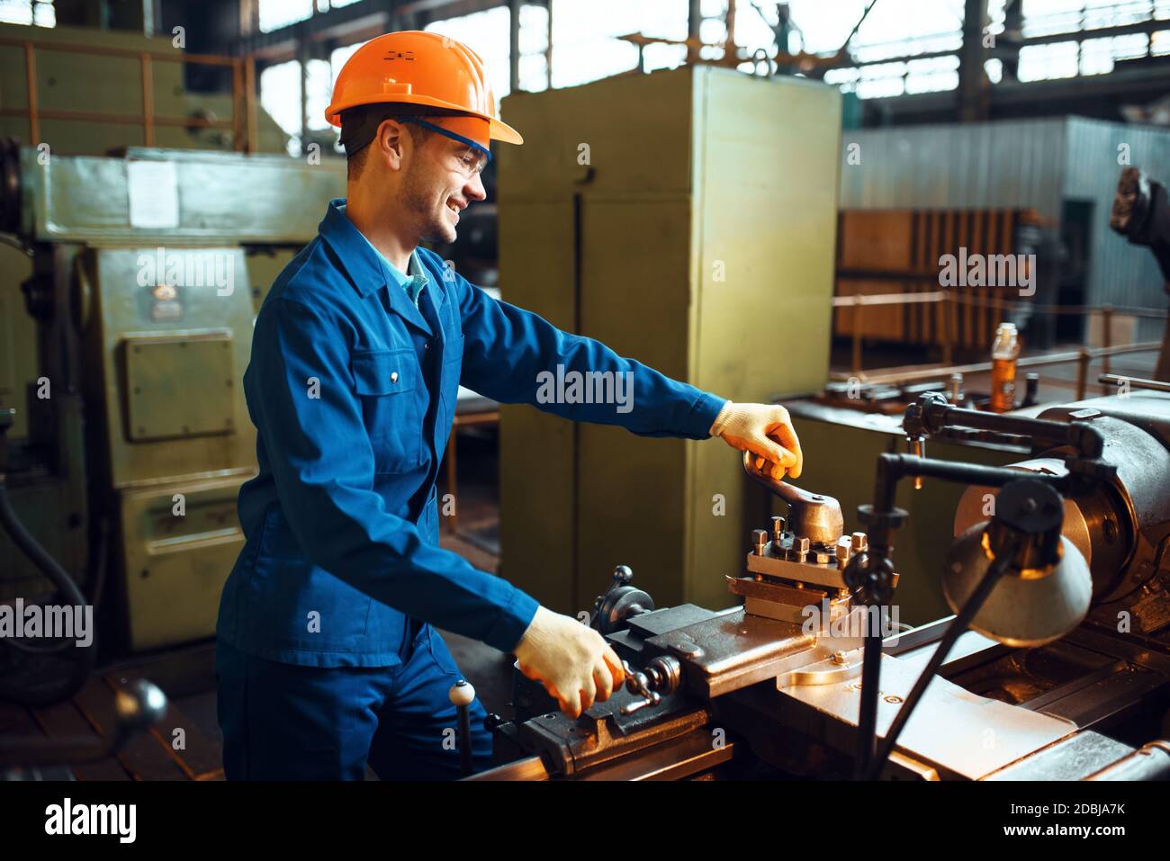 Worker in uniform and helmet works on lathe, factory. Industrial ...