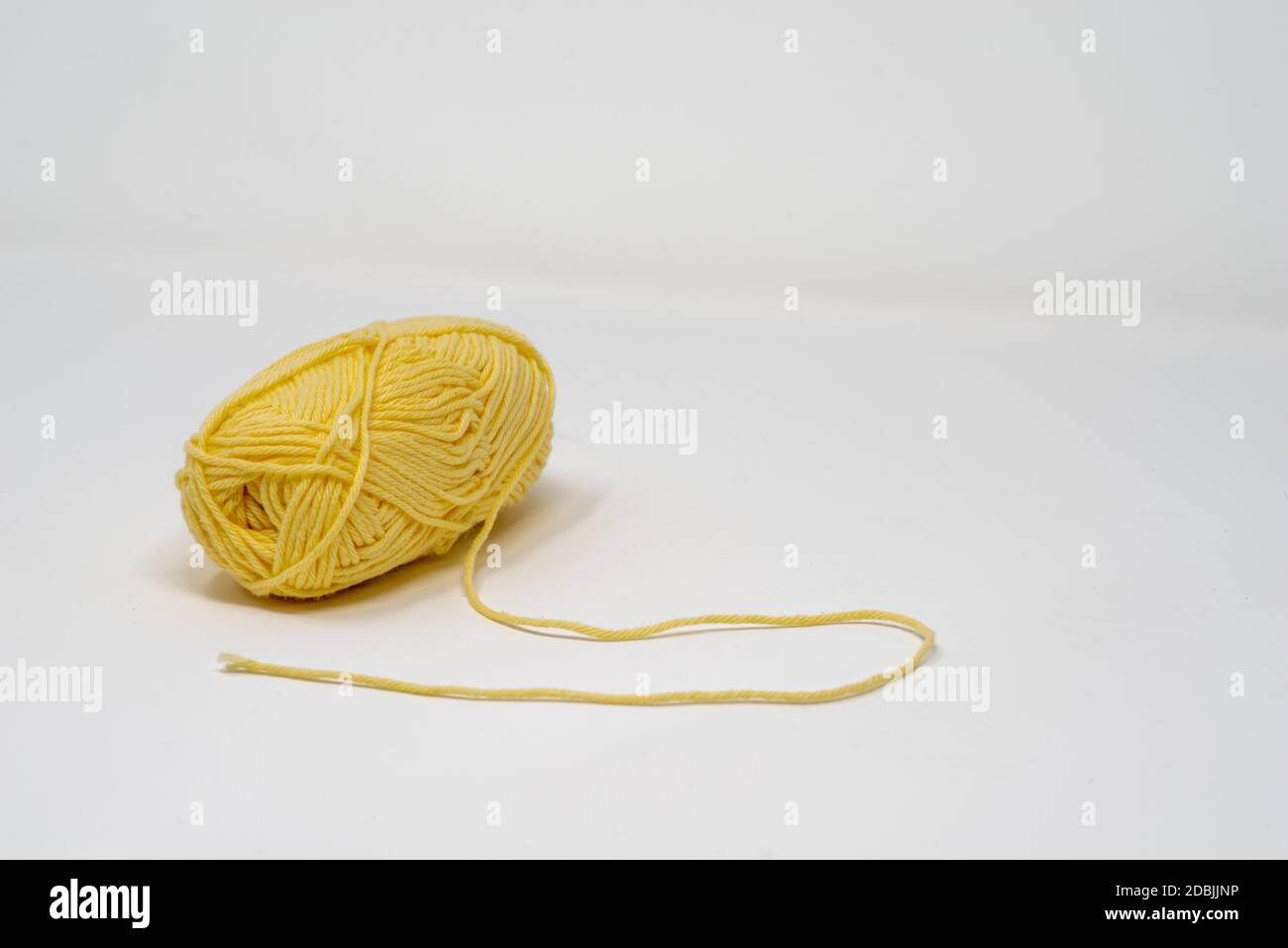 Single ball of wool with a trailing yellow end with a plain white ...