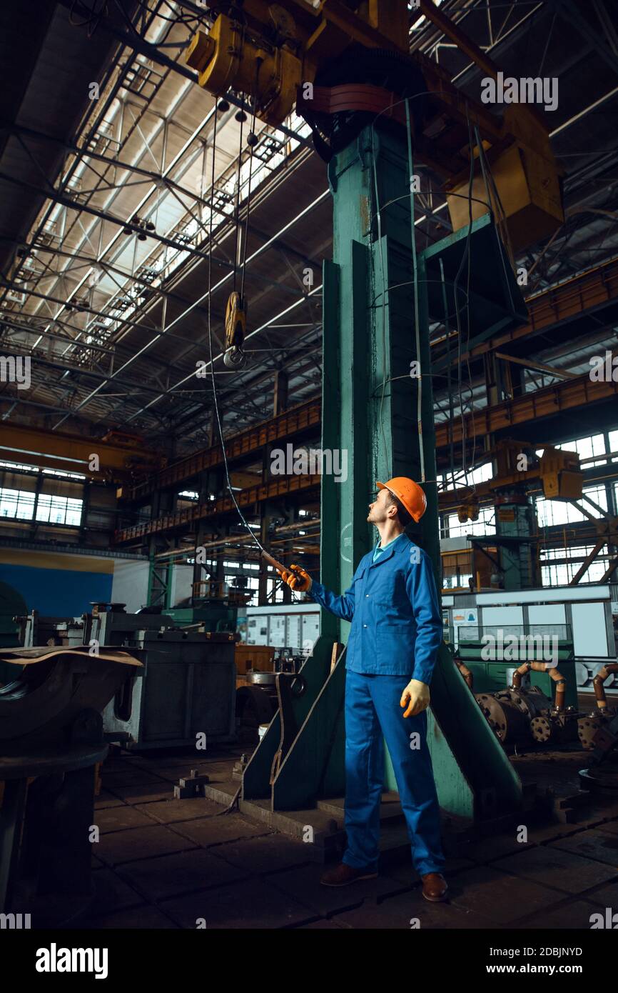 Male worker in uniform and helmet operates a crane on factory ...