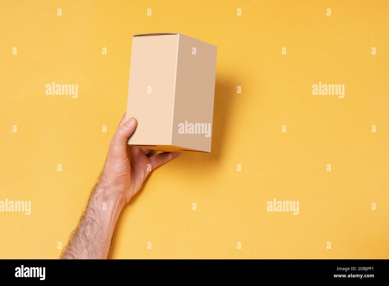 Male hand holding a small box in front of yellow background, mock-up ...