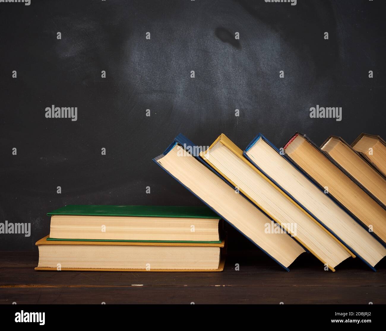various hardback books on the background of an empty black chalk board ...