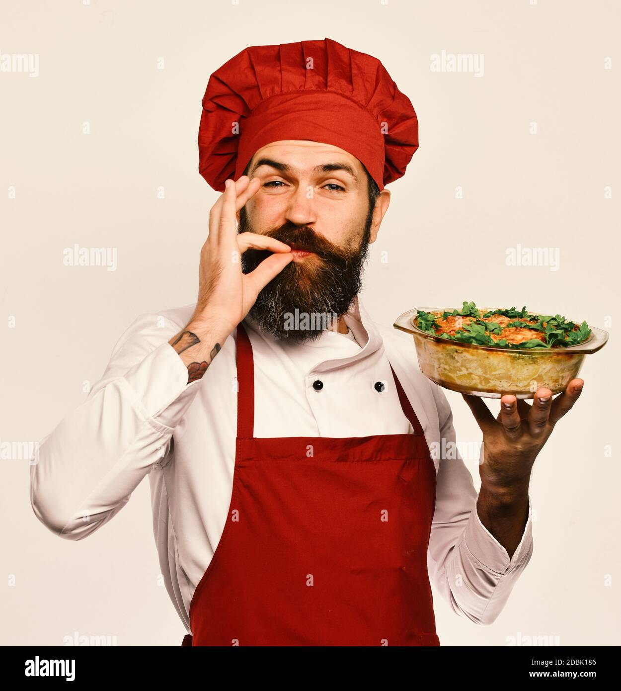 Cook with happy face in burgundy uniform holds baked dish. Man with ...
