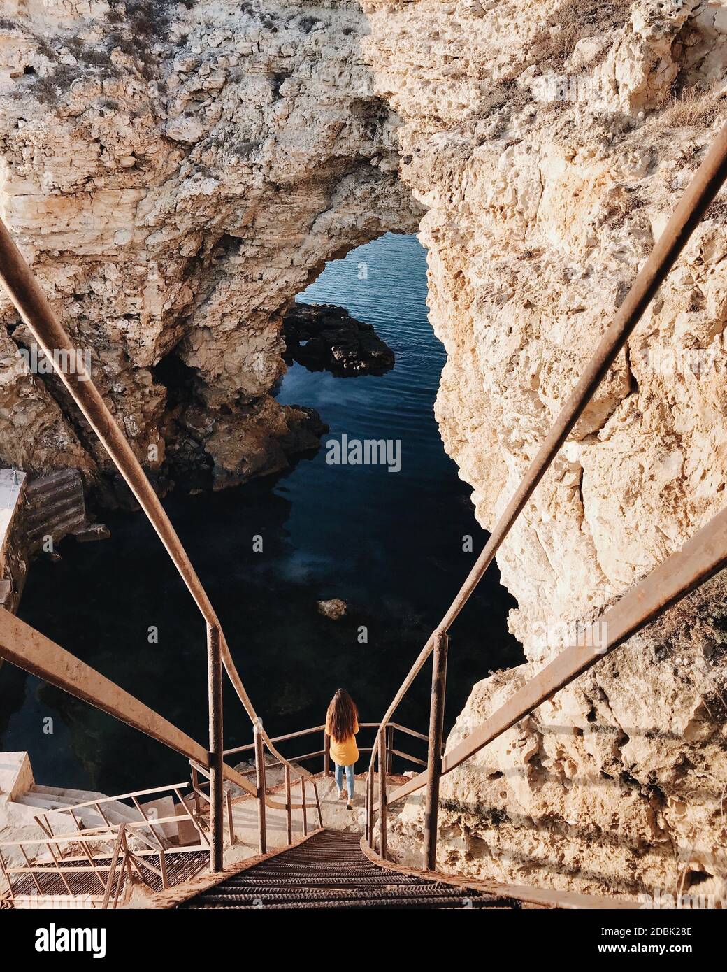 Girl traveler in a yellow coat waiting in the blue sea bay. Geometric ...