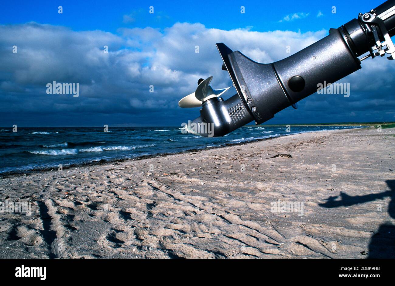 On a beach with large cloud formations and stormy seas, an outboard ...
