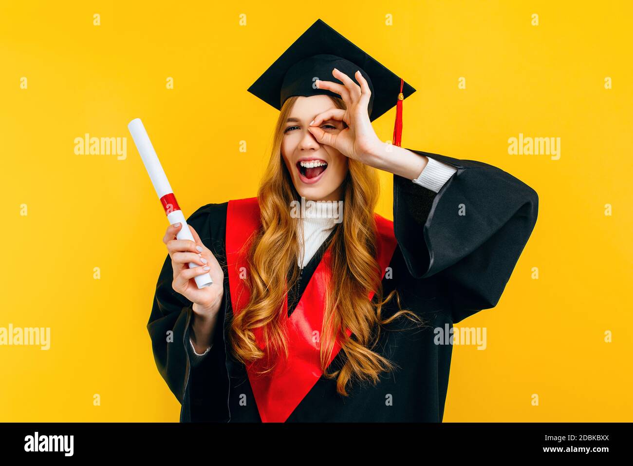 An attractive graduate shows an OK gesture and winks with a diploma on ...