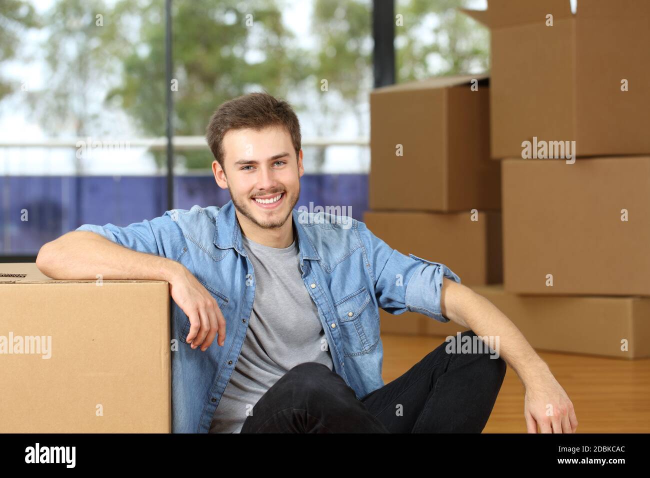Happy man moving home looking at camera posing sitting on the floor ...