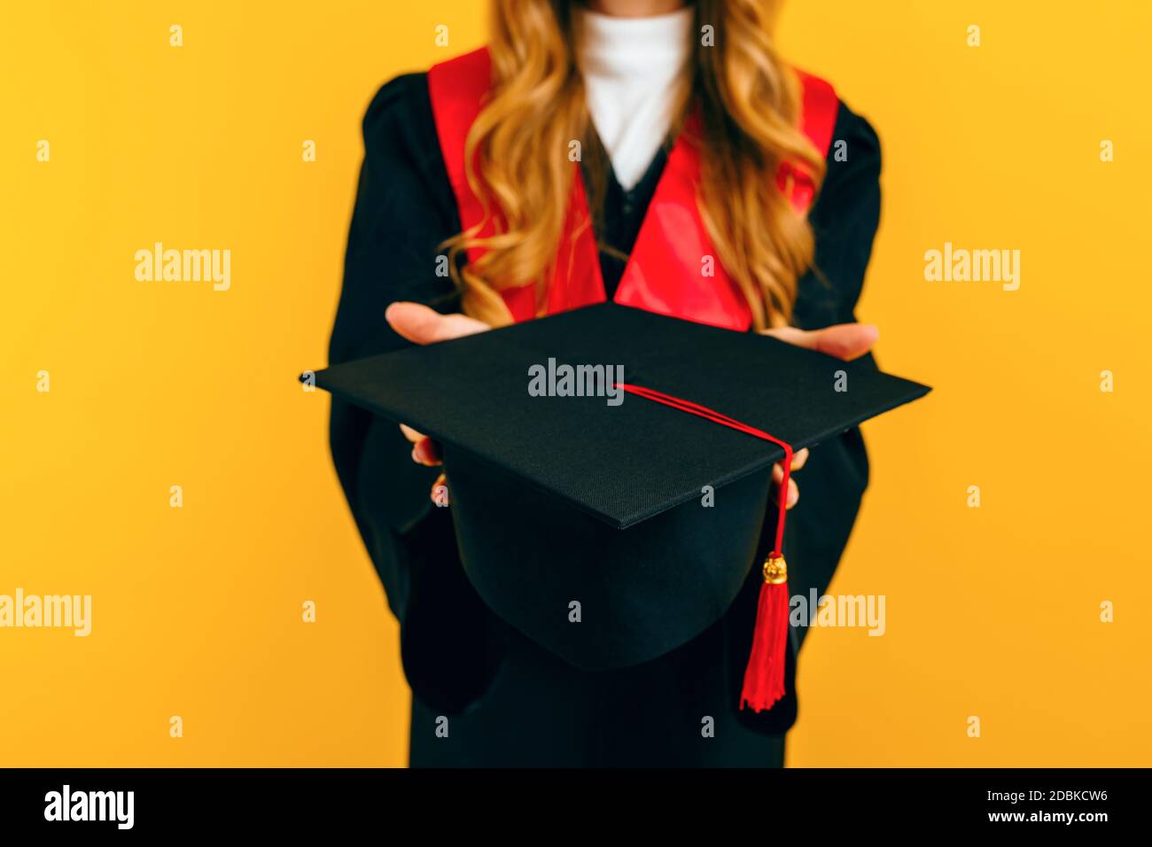 Student with a graduation hat in hand, on a yellow background, close-up ...