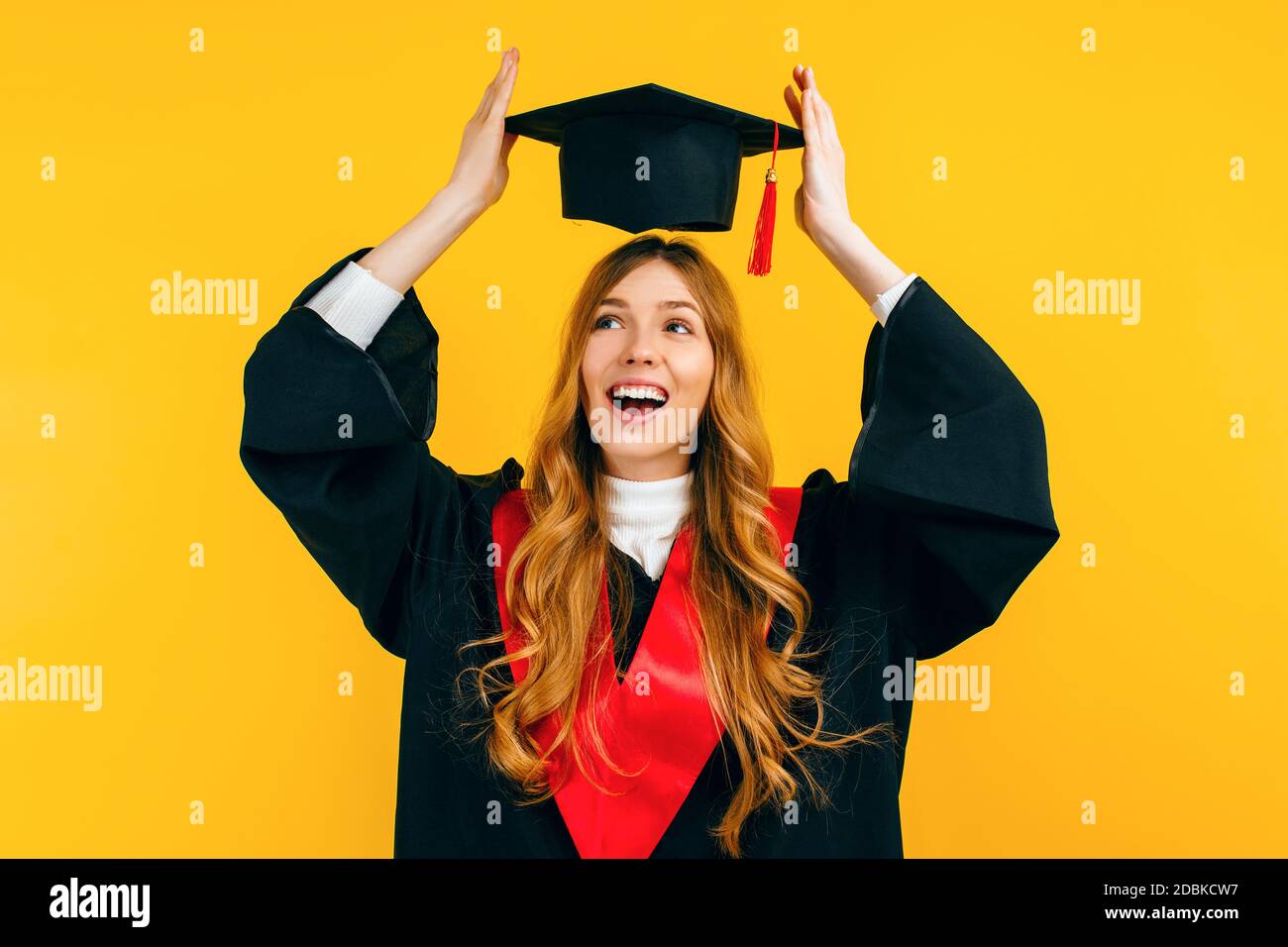Happy attractive graduate, puts a graduation cap on her head, on an ...