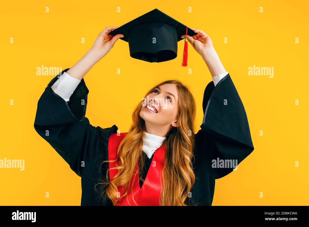 Happy attractive graduate, puts a graduation cap on her head, on an ...